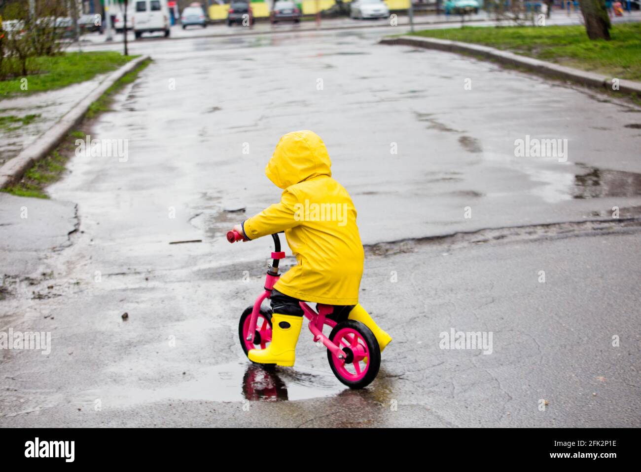 little girl in yellow raincoat rides on bike ride through puddles in ...