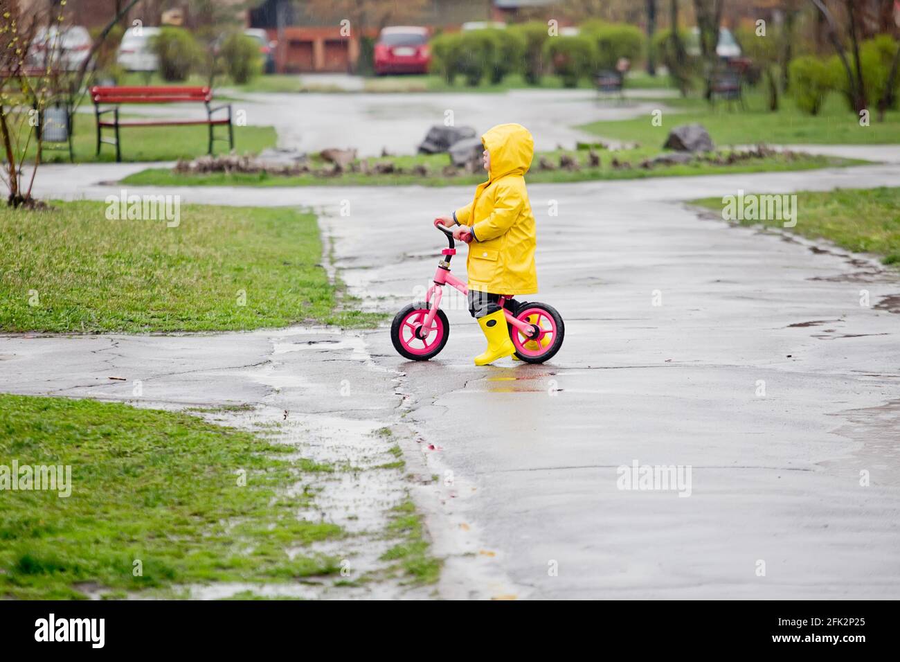 little girl in yellow raincoat rides on bike ride through puddles in ...