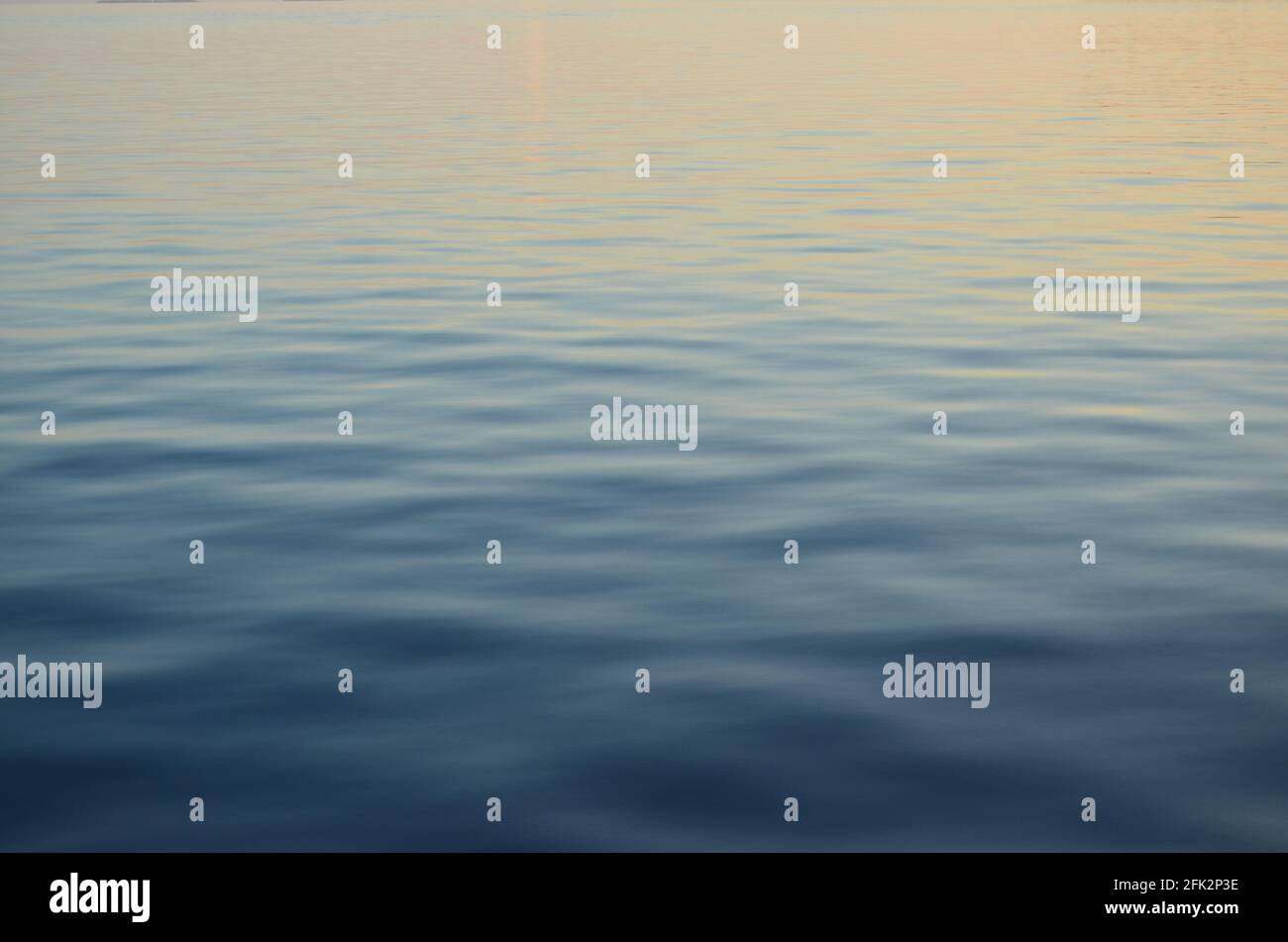 Background of water tides with sunset colors visible in the reflection ...