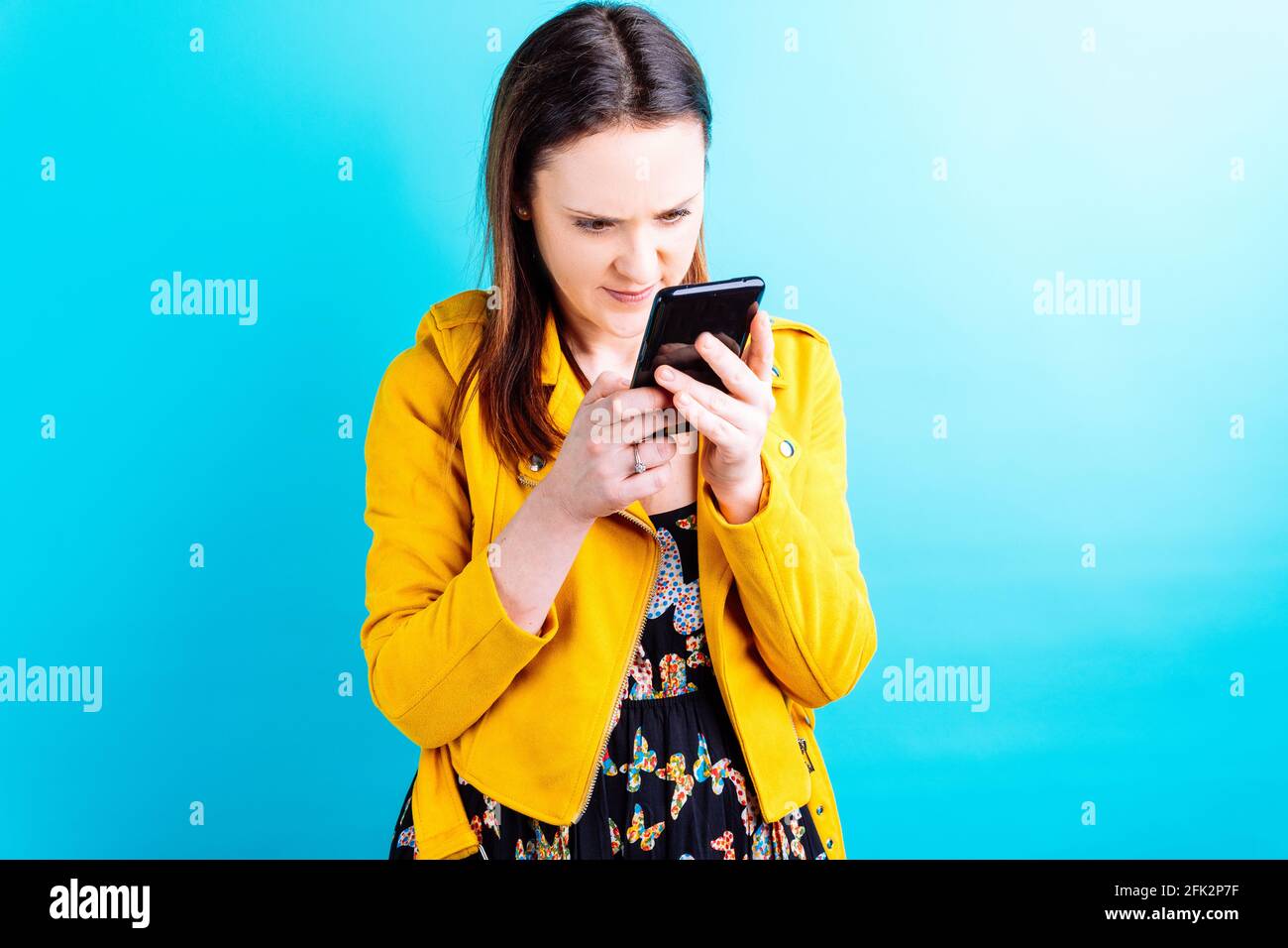 Beautiful young adult woman in yellow jacket on blue background looking ...