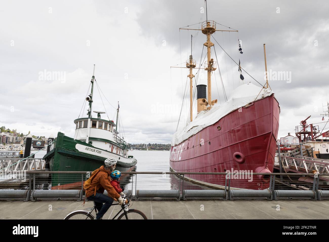 A cyclist with a small child rides past the Arthur Foss tugboat and the ...