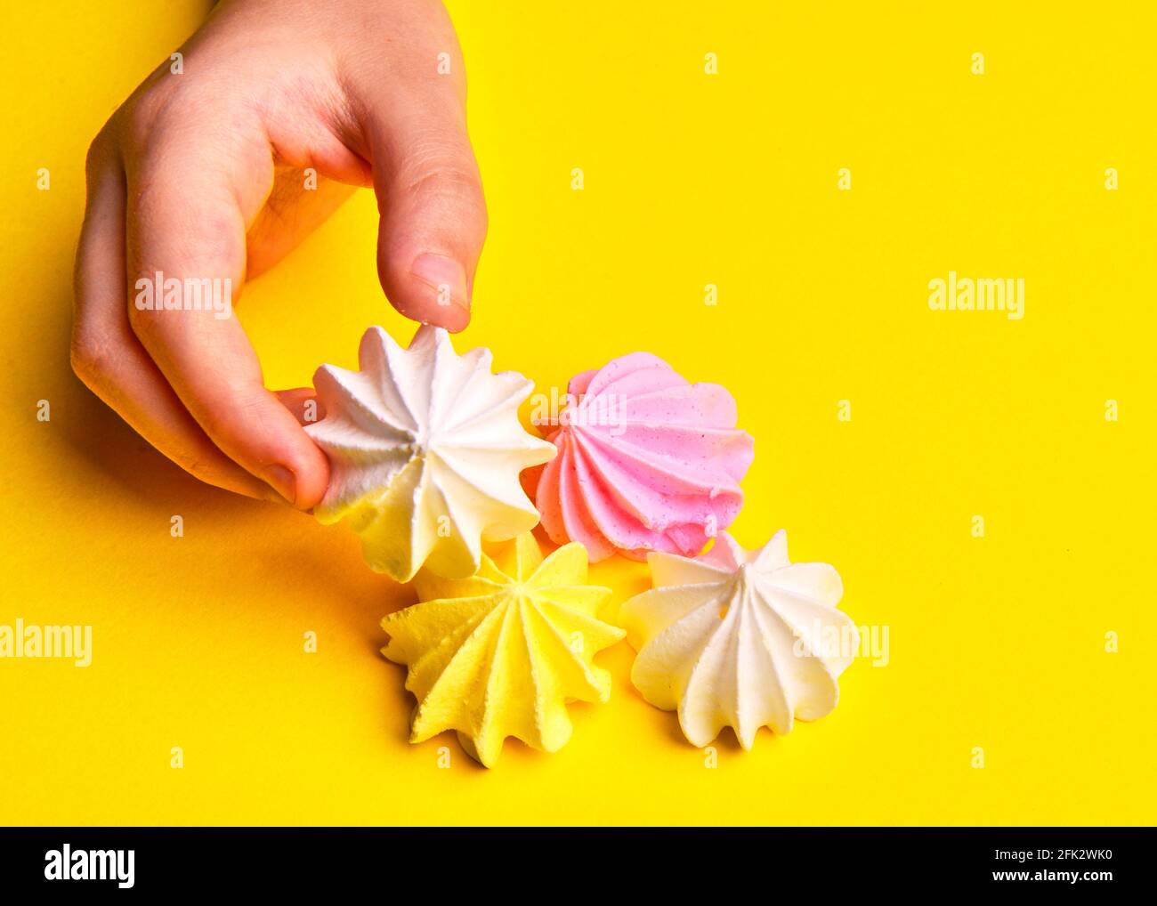 colored meringues in hand on bright yellow background Stock Photo - Alamy