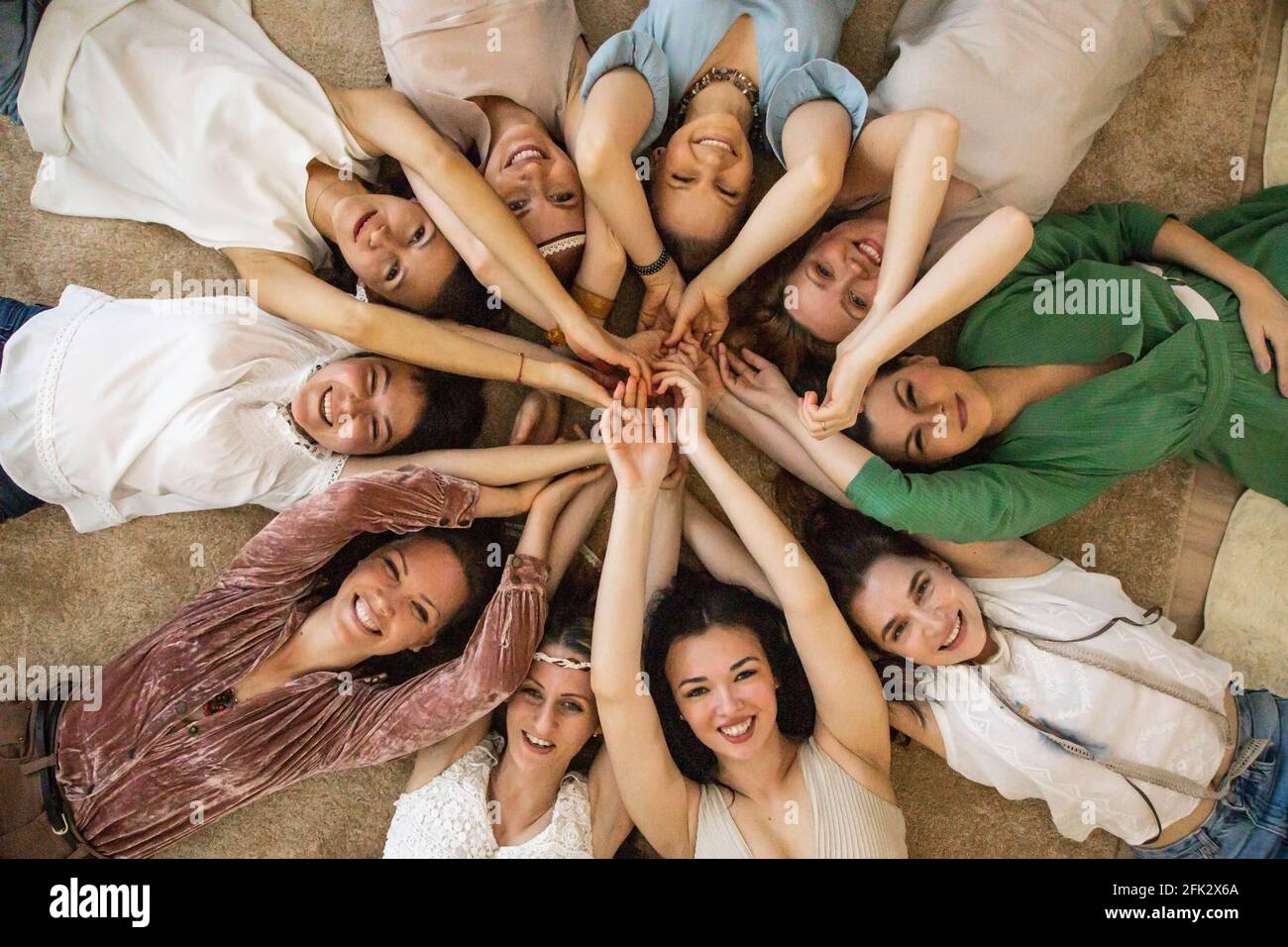 Happy female friends lying circle raising hands together enjoying ...