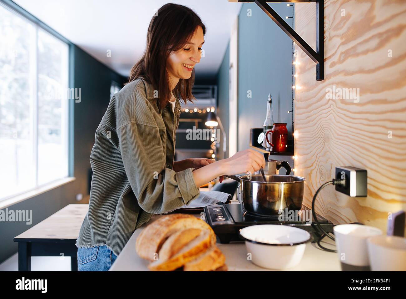 Smiling woman cooking on a high kitchen table, she's stirring soup on a ...