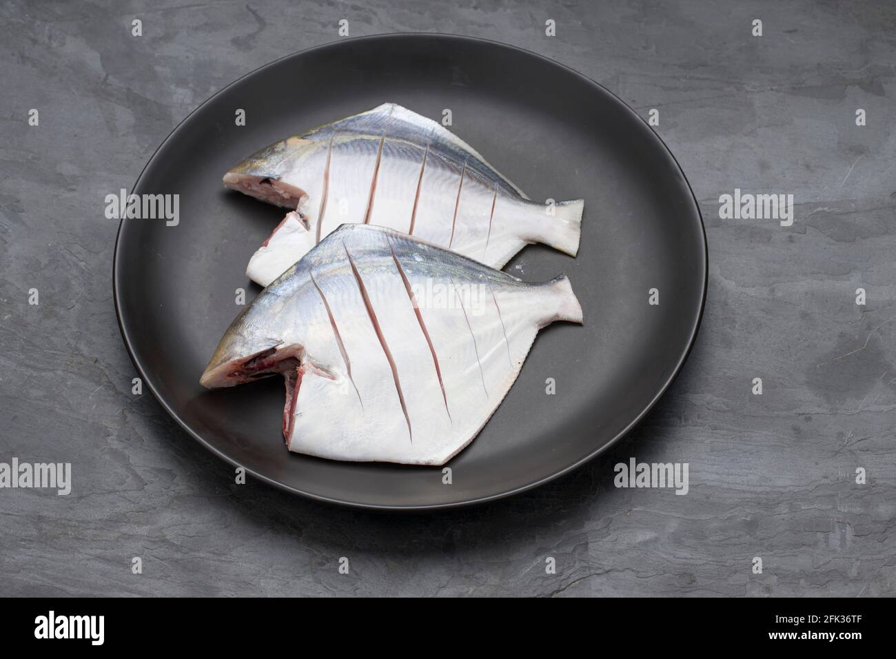 Raw white pomfret, ready to cook pomfret arranged in a black plate with ...