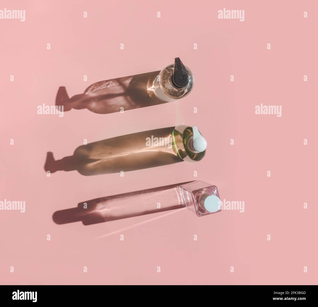 Three cosmetic product bottles in sunlight with shadow on pink ...