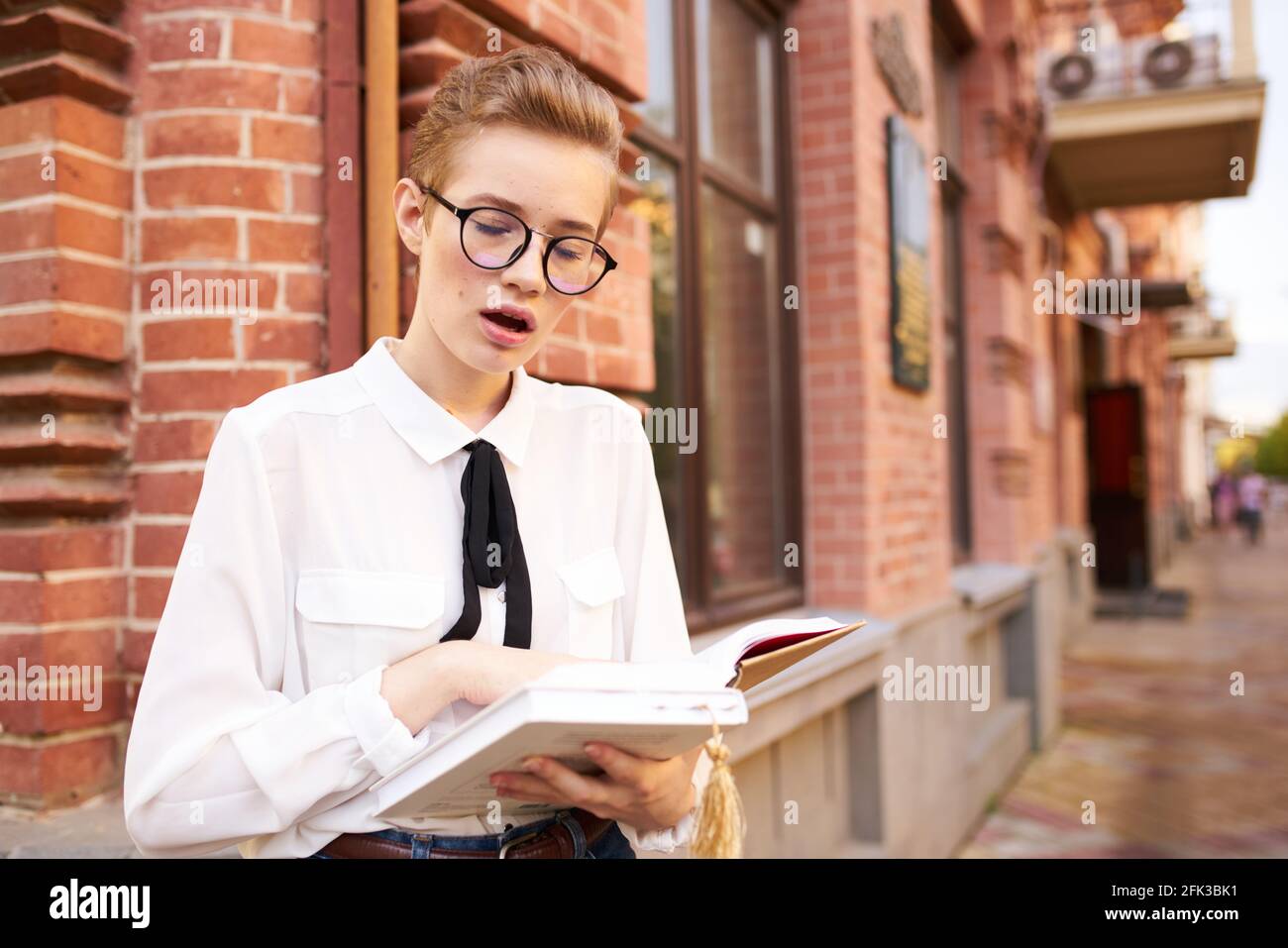woman reading book on the street near brick building and notebook ...