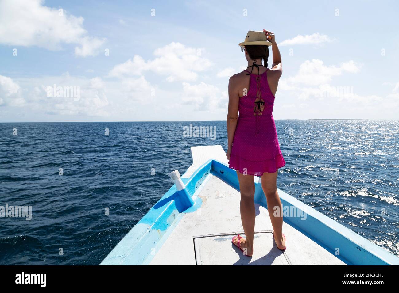 Woman holds her hat while standing on the deck of a wooden boat in the ...