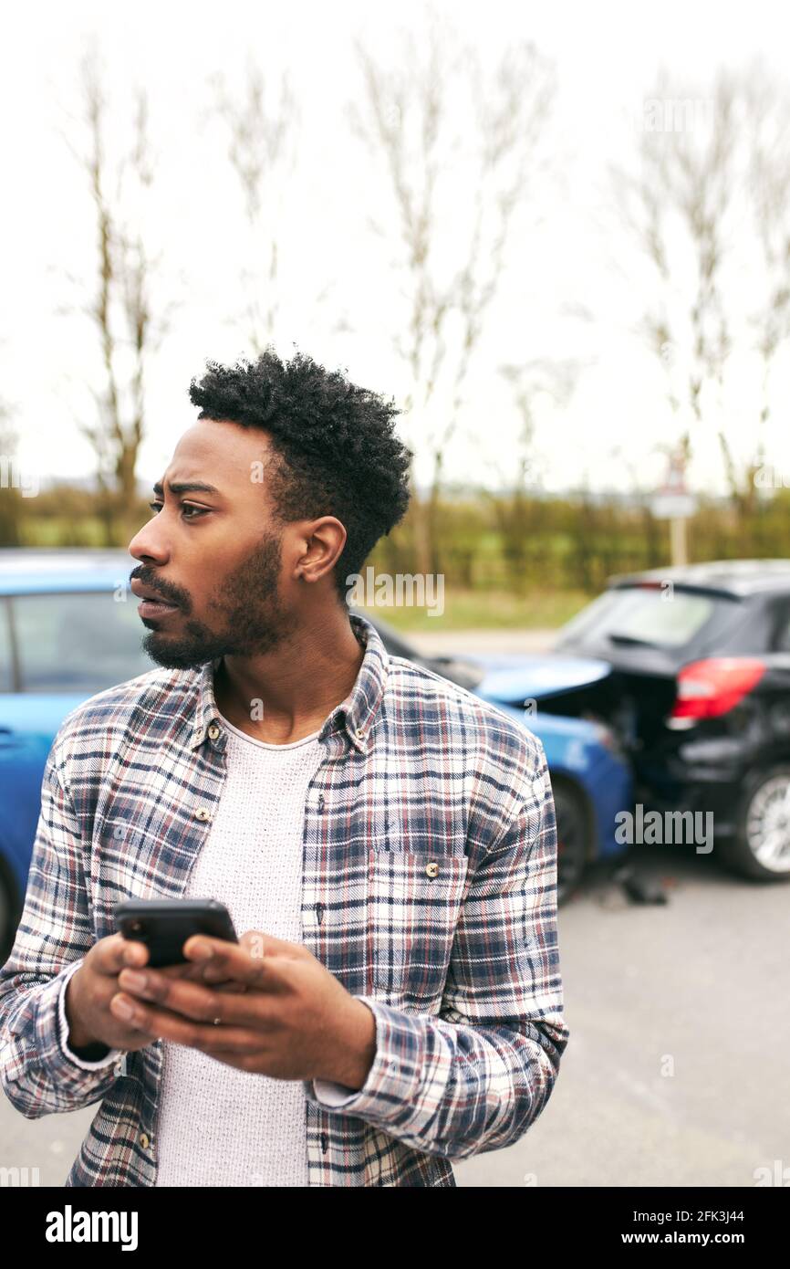 Young man standing by damaged car after traffic accident calling ...