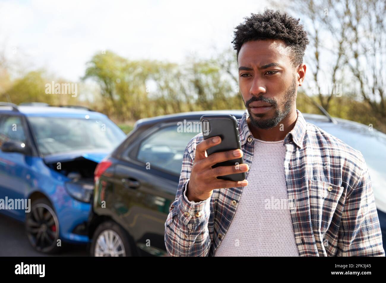 Young man standing by damaged car after traffic accident calling ...
