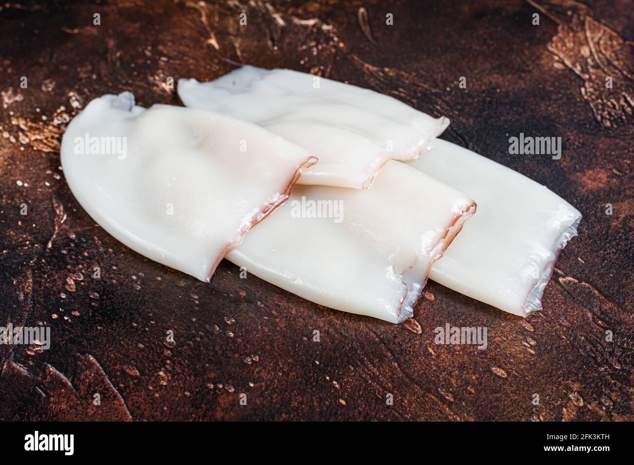 Raw Squid or Calamari tubes on a kitchen table. Dark background. Top ...