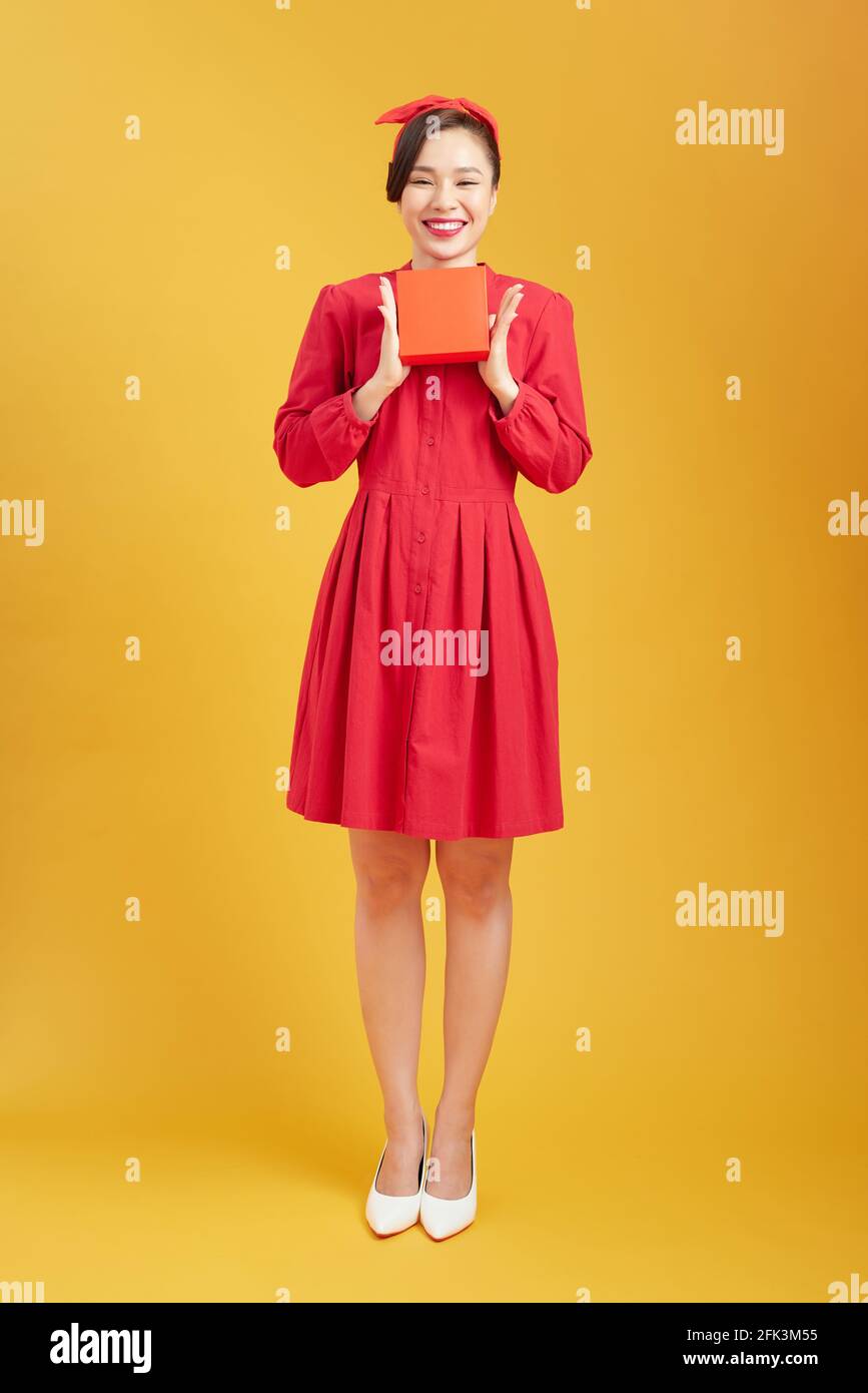 Beautiful cheerful woman in red dress giving you red gift over yellow ...