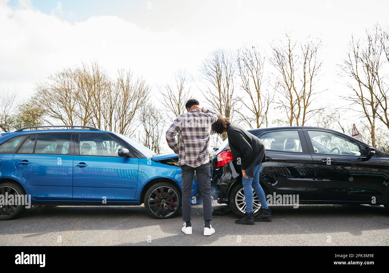 Young male and female drivers looking at damaged car hit from behind ...