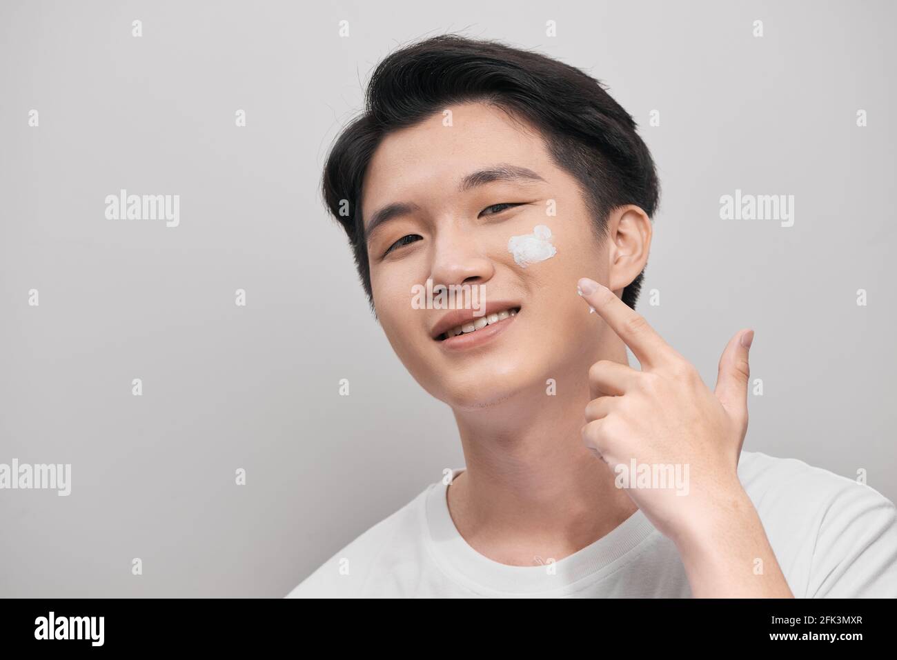 Skin care. Portrait of handsome young man applying cream to his face ...