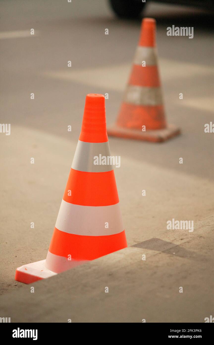 Two safety cones on asphalt road. New cone on front in focus, old on ...