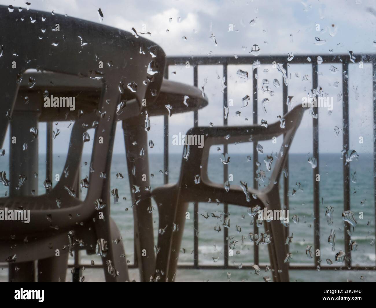 Empty terrace in a beachside apartment, seen from behind rain-splashed ...