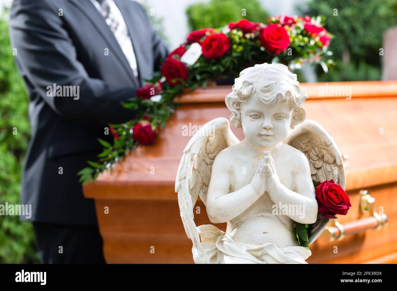 Mourning man on funeral with red rose standing at casket or coffin ...