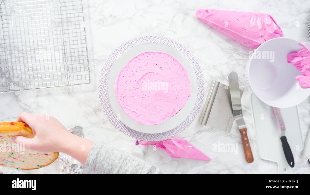 Flat lay. Step by step. Frosting round funfetti cake layers with pink ...