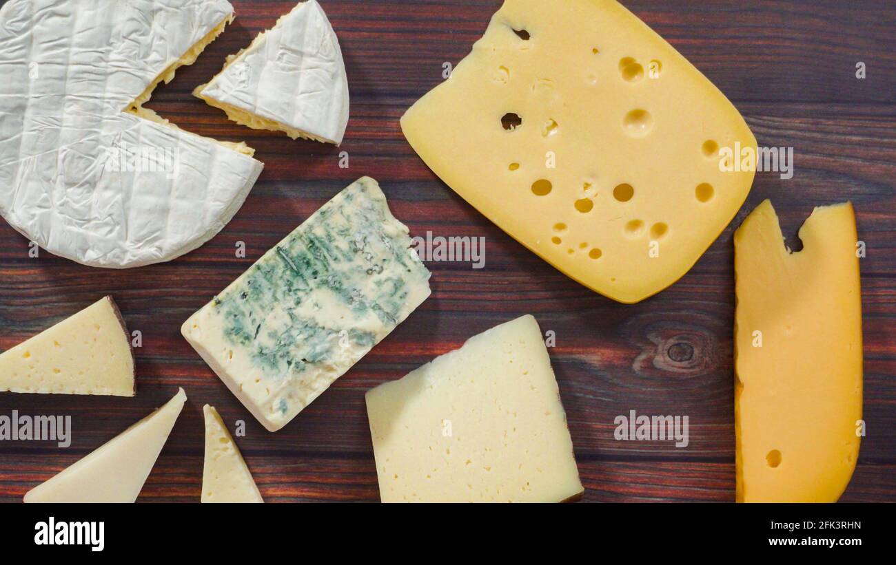 Flat lay. Large wedges of gourmet cheese on a rustic wood background ...