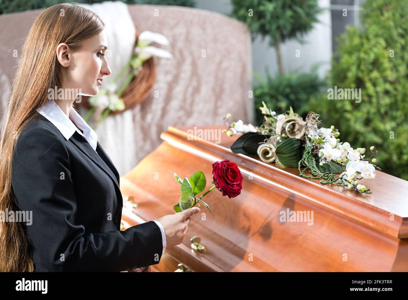 Mourning woman on funeral with red rose standing at casket or coffin ...
