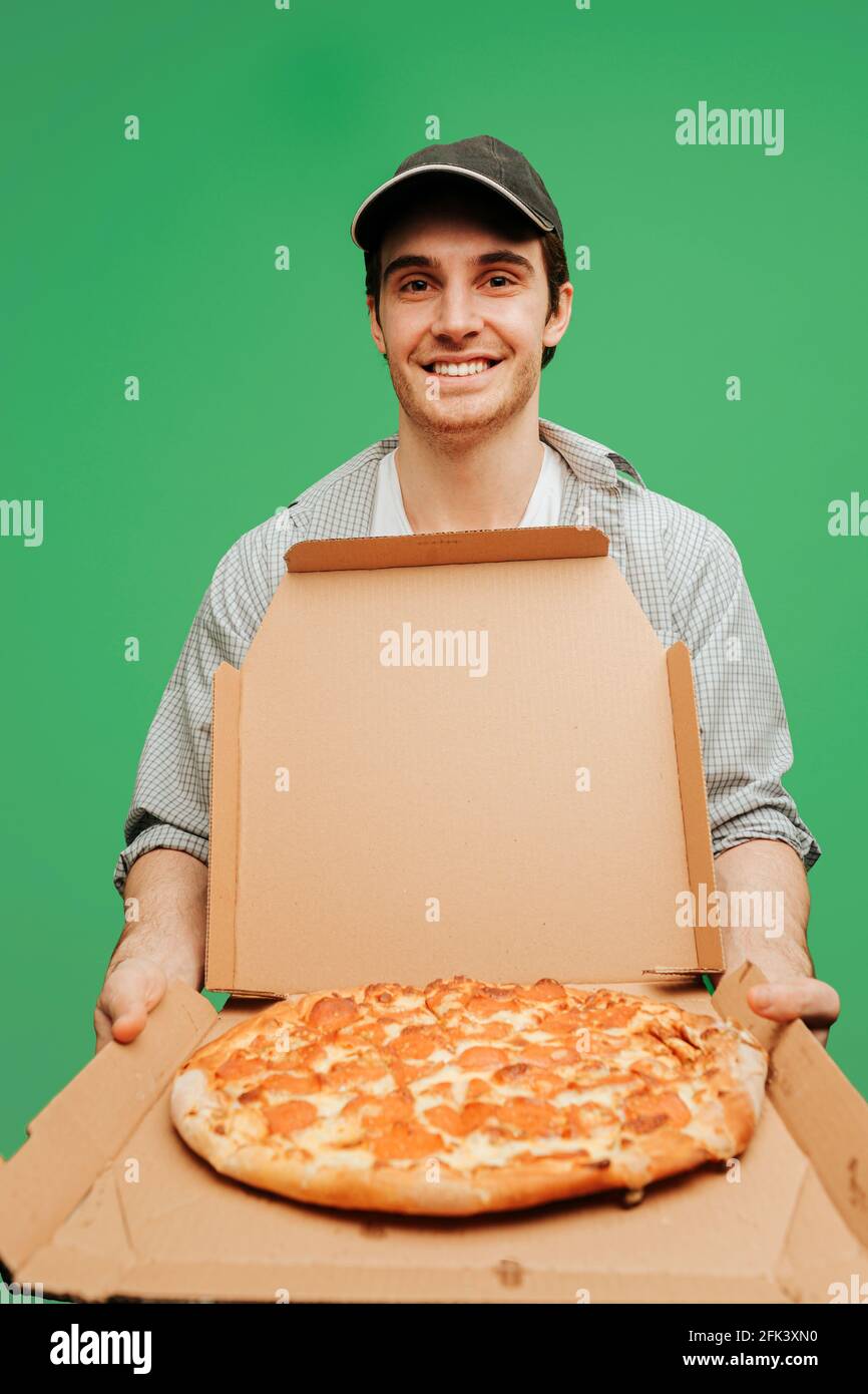 Nice pizza deliveryman opens box with pizza, isolated on green ...