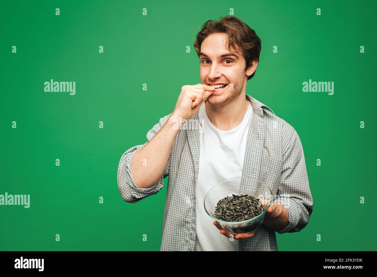 Young man eats sunflower seeds, isolated on green background Stock ...