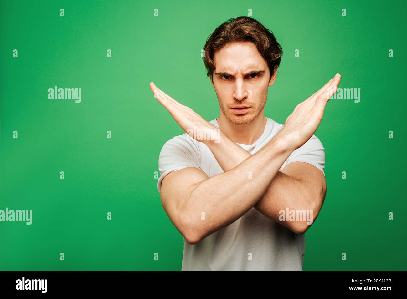 Young man looks seriously and shows not allowed, isolated on green ...