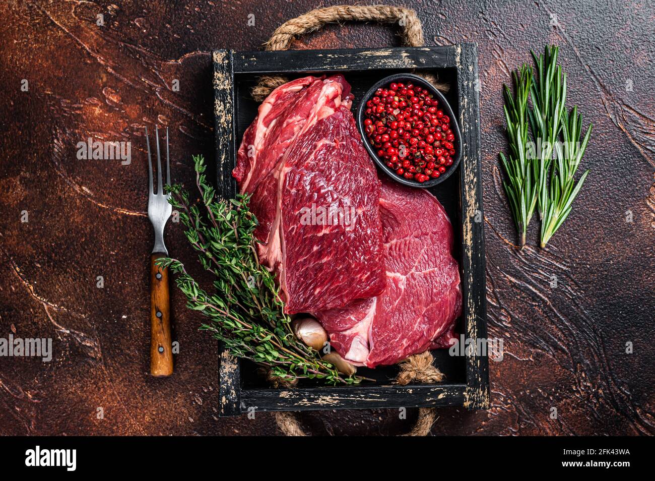 Raw rib eye beef steak in a wooden tray with herbs. Dark background ...
