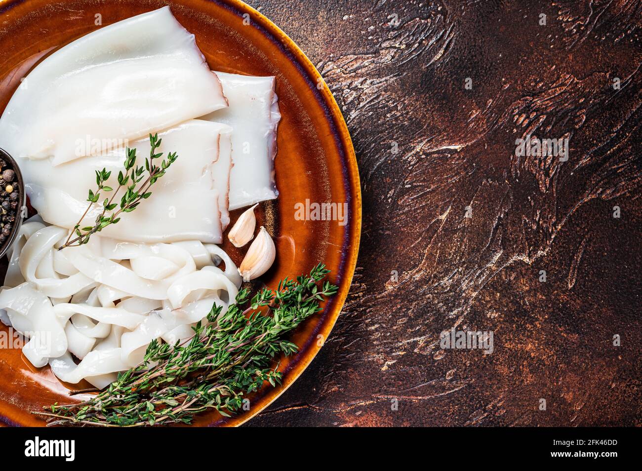 Sliced raw rings squid in a rustic plate with rosemary. Dark background ...