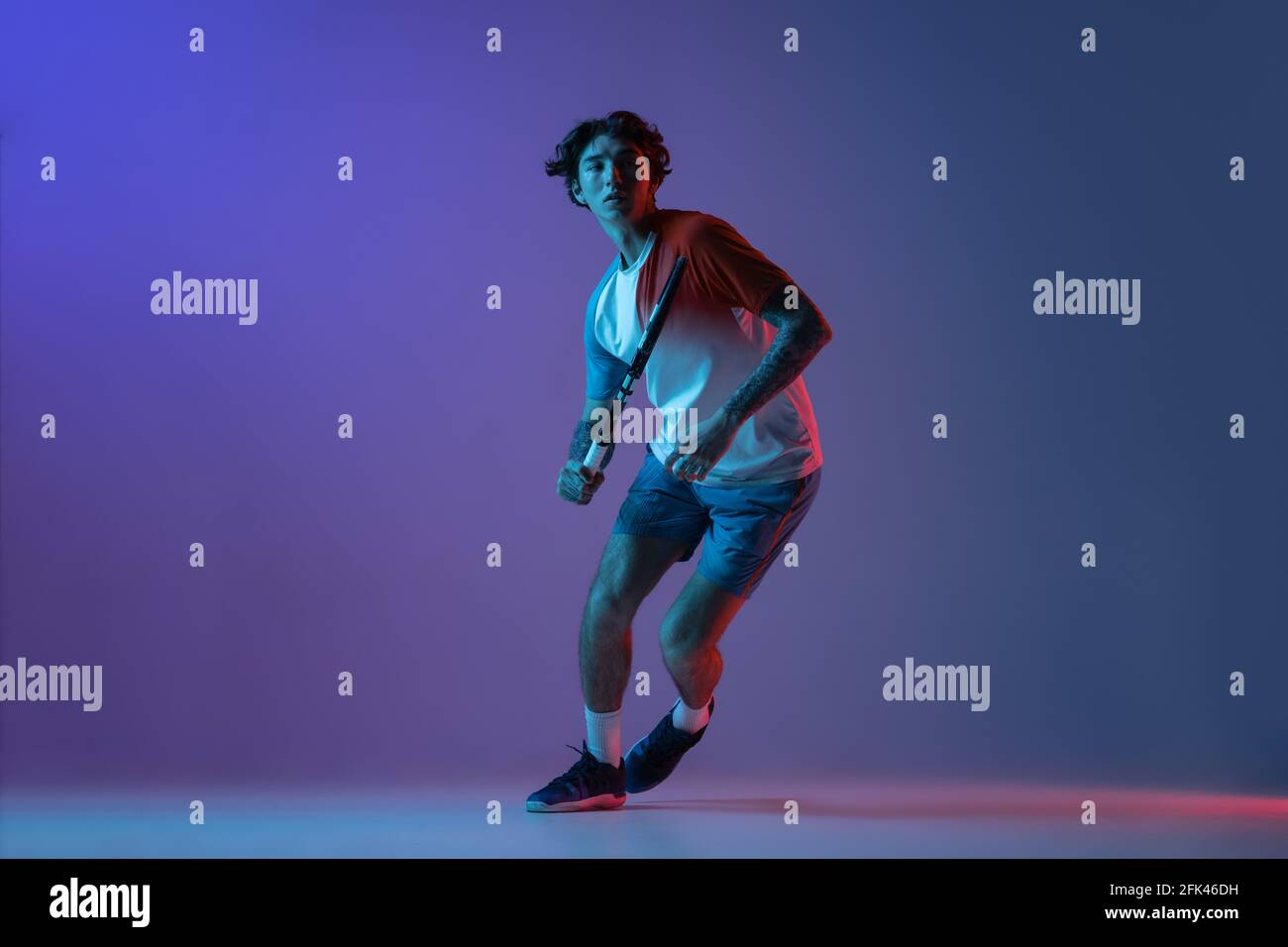 Young caucasian man playing tennis isolated on purple-blue studio ...