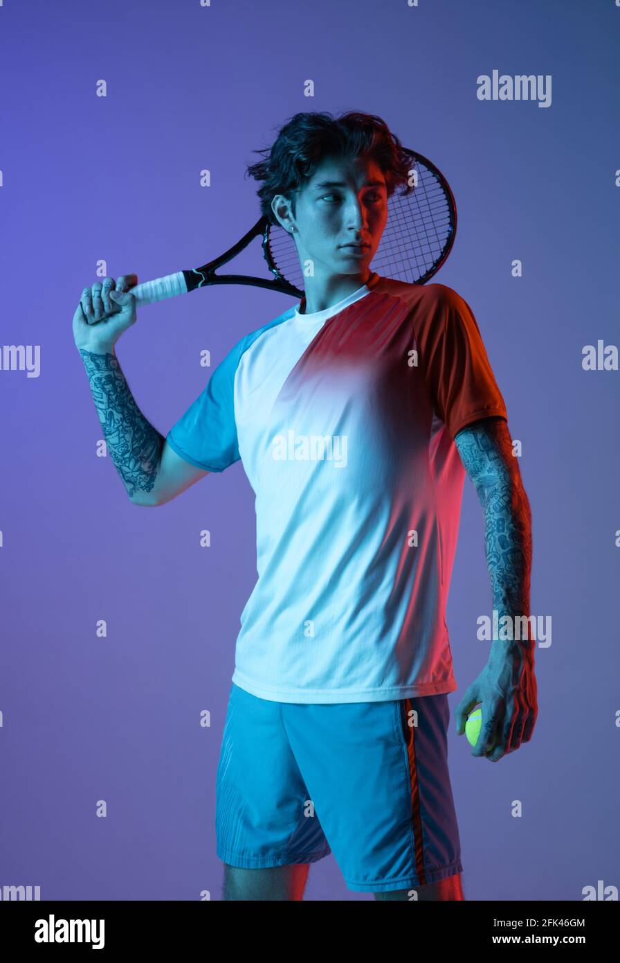 Young caucasian man playing tennis isolated on purple-blue studio ...