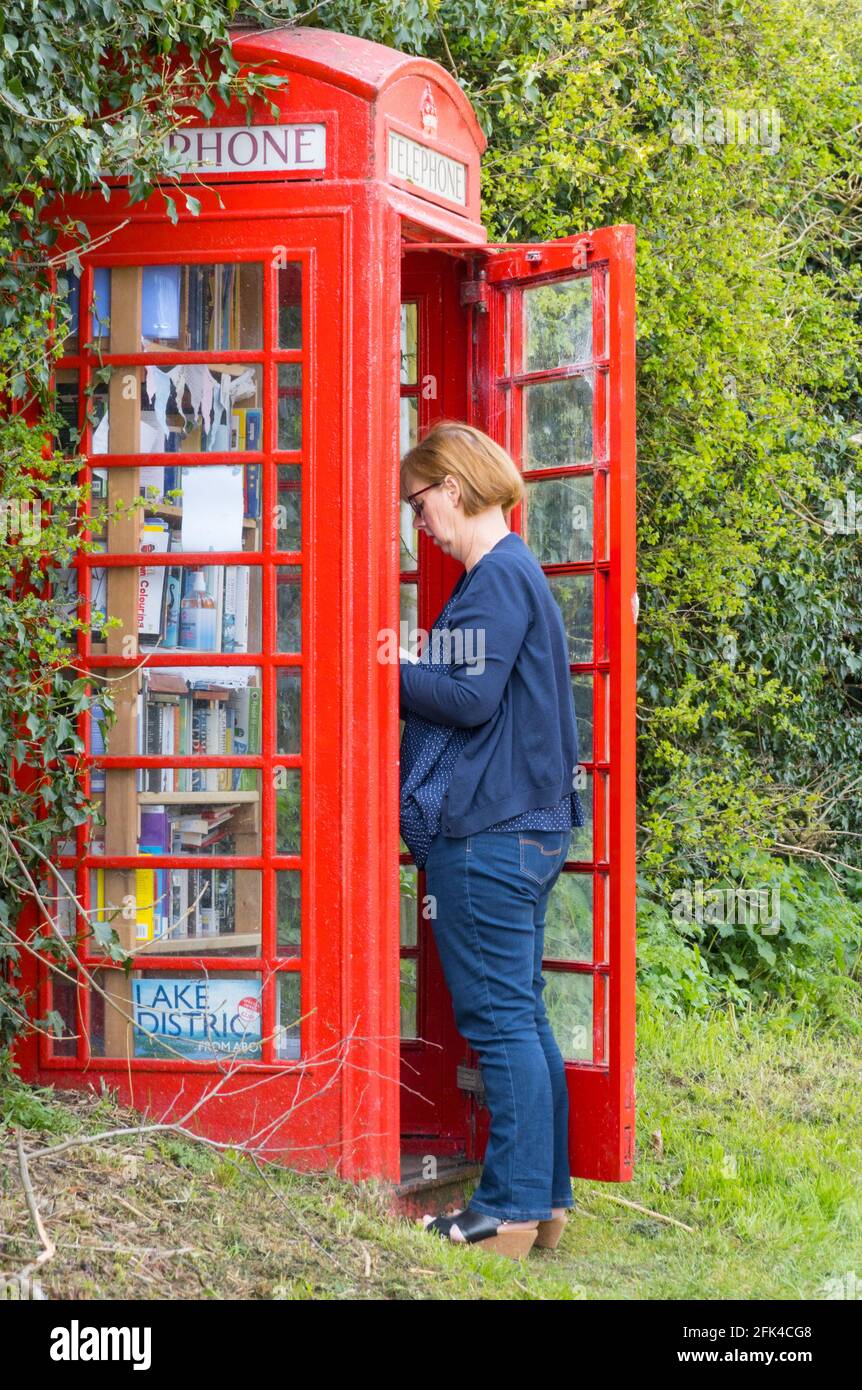 Woman selecting books from an old red telephone box, which is now being ...