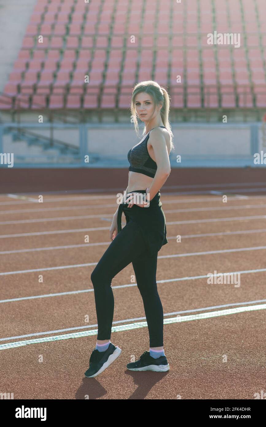 A female coach with dark hair stands on the red running track of the ...