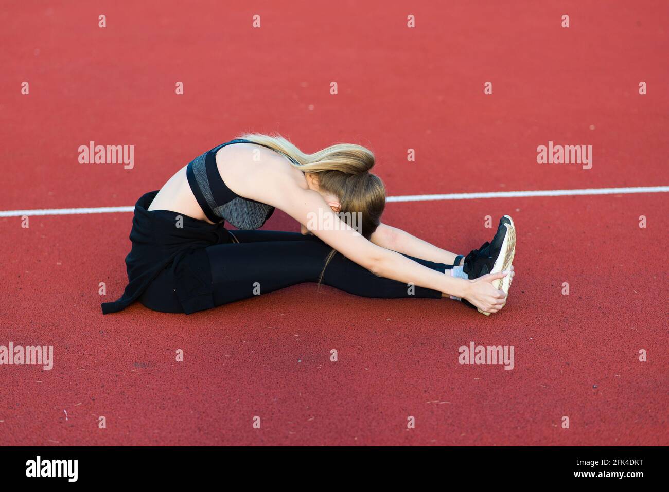 A female coach with dark hair stands on the red running track of the ...