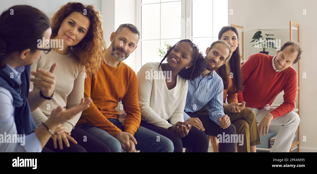 Group of interracial people sit in a row and listen with interest to a ...
