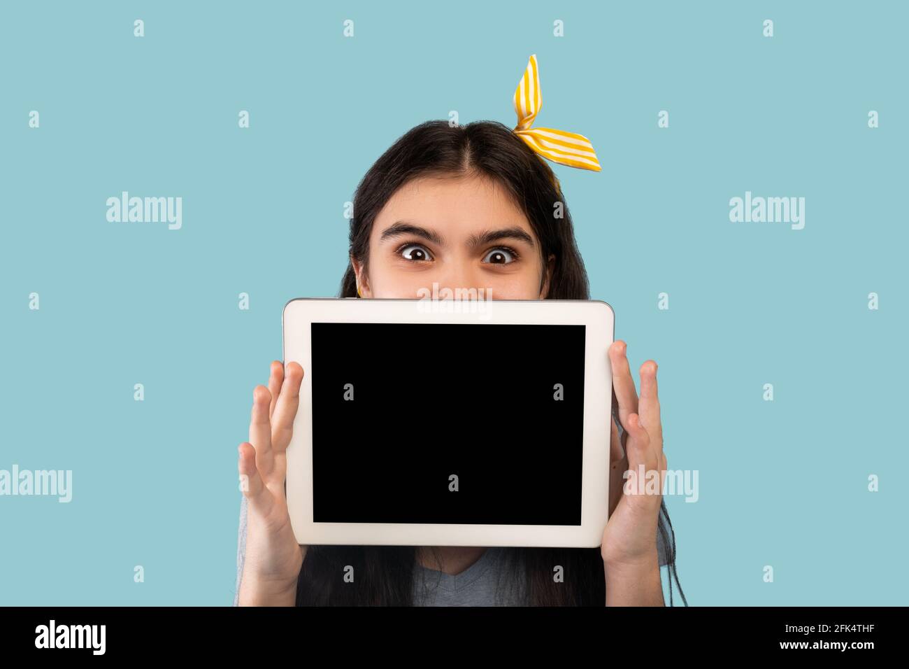 Indian adolescent girl hiding behind tablet pc with blank screen on ...