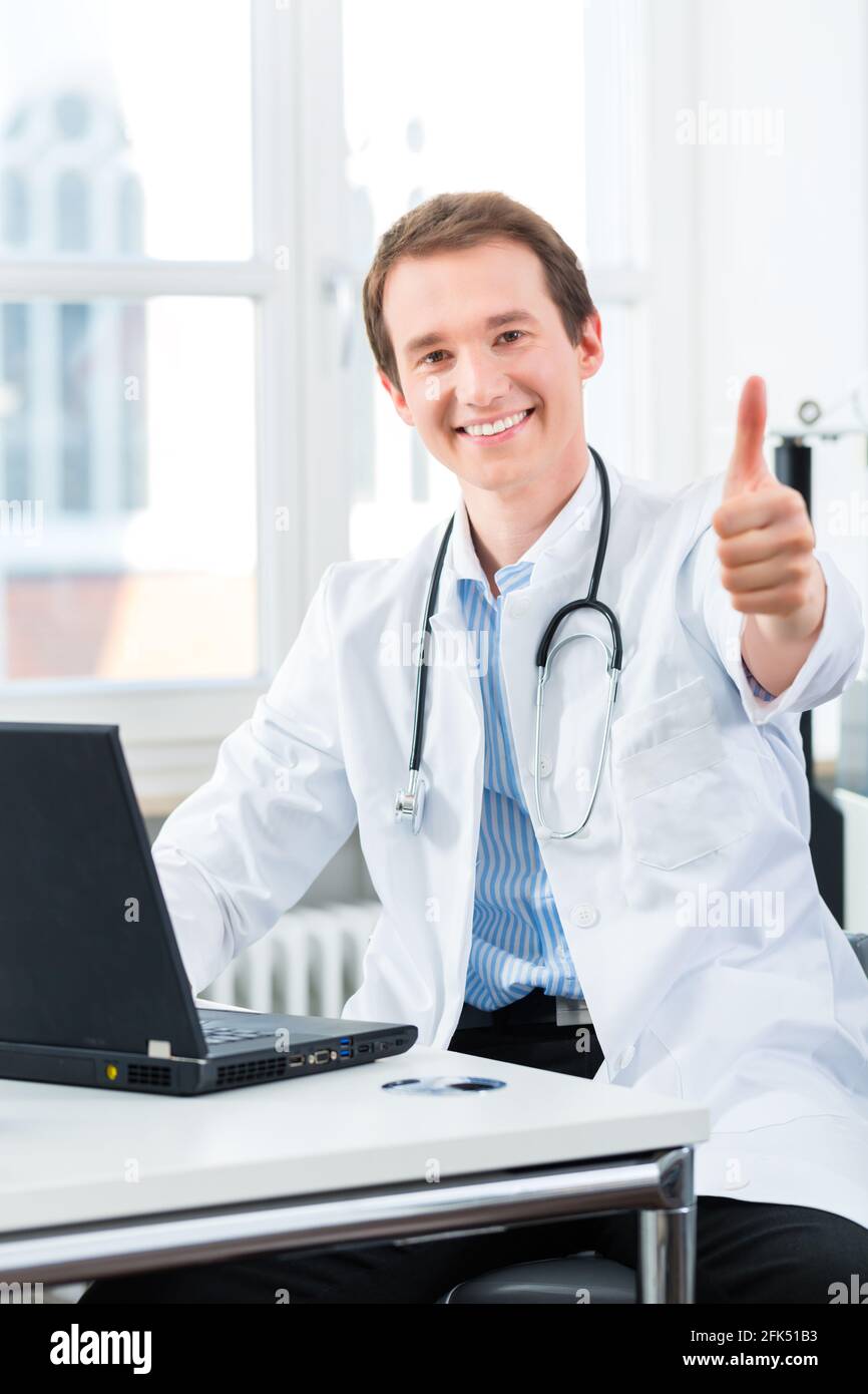 Young doctor sitting at a desk in front of window in clinic on a ...