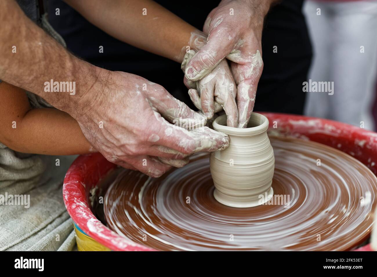Closeup hands of the potter and his young apprentice create a vase on a ...