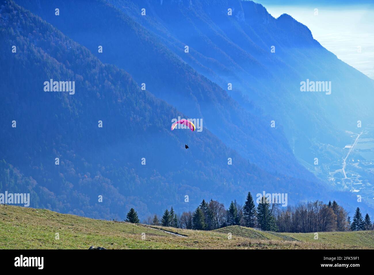 A paraglider taking off over a valley with a dramatic backdrop of ...