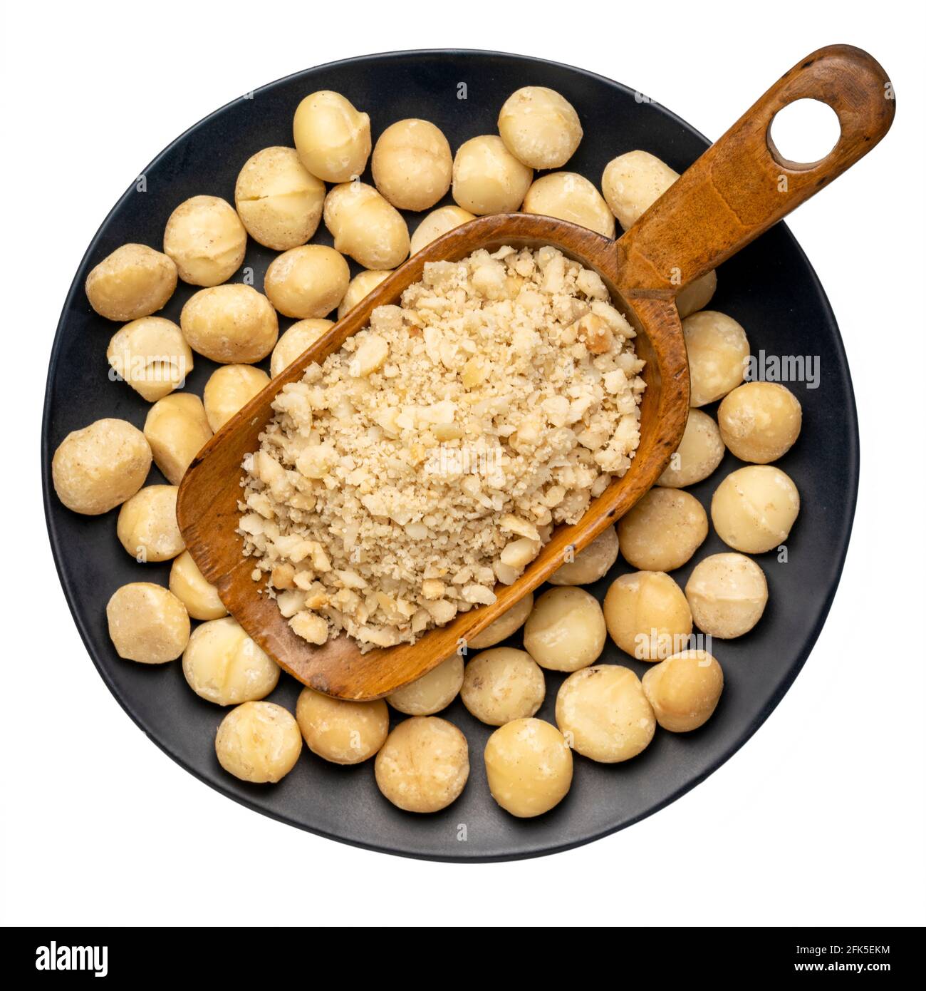 macadamia nut flour in wooden scoop on a black ceramic plated isolated ...