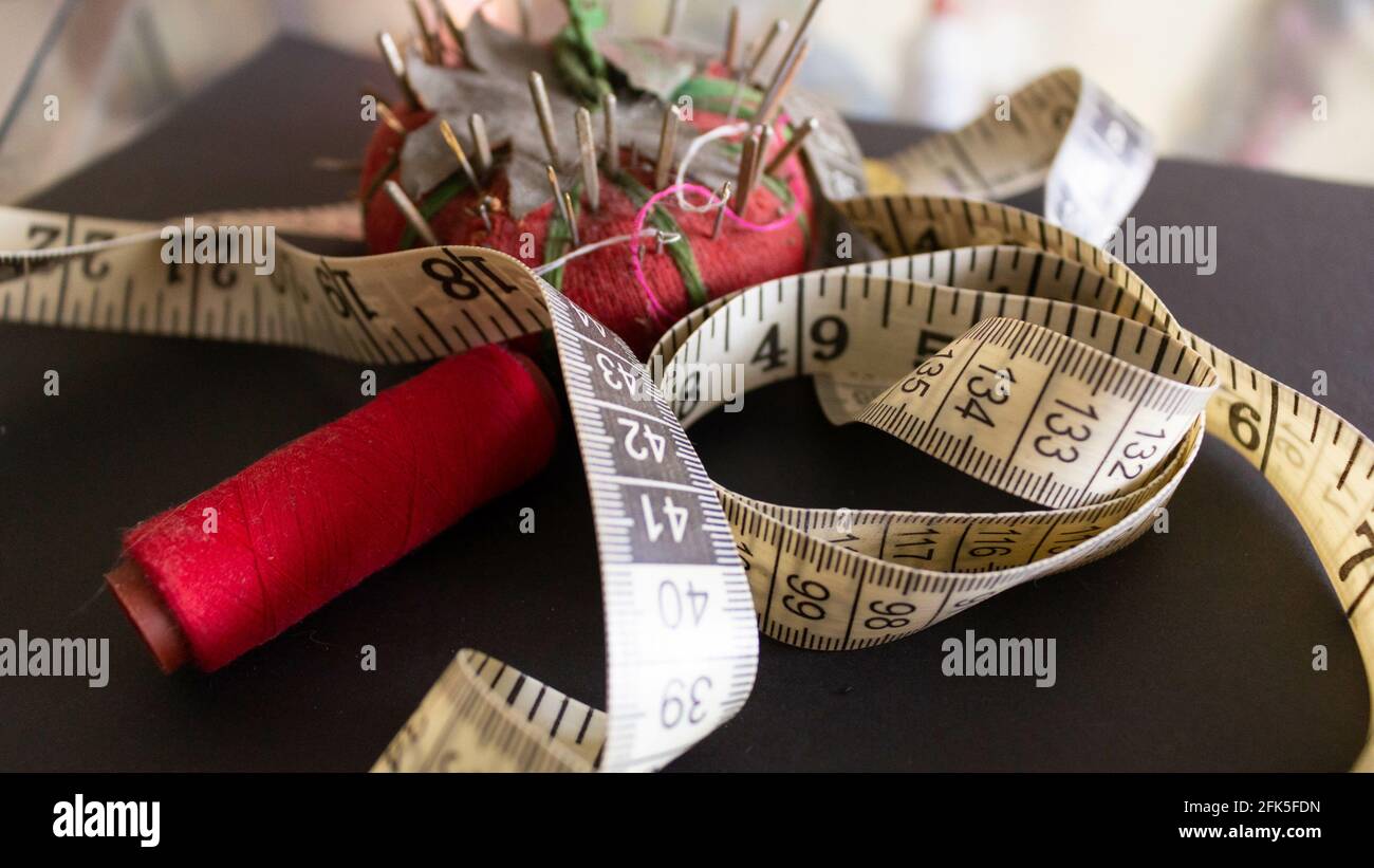 Measuring tape, spool of thread and needles on a black surface Stock ...