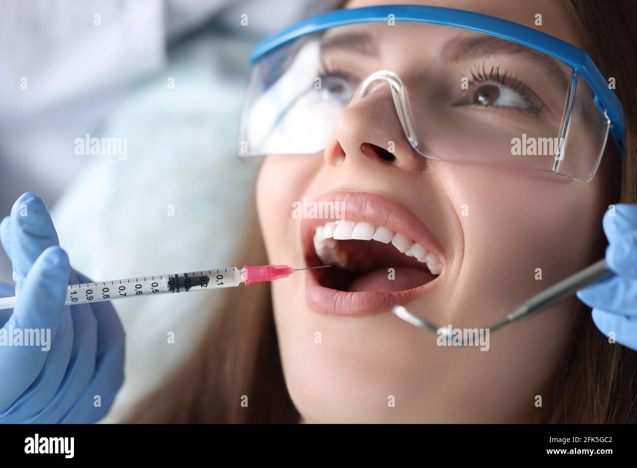 Dentist making injection in gum of female patient in clinic Stock Photo ...