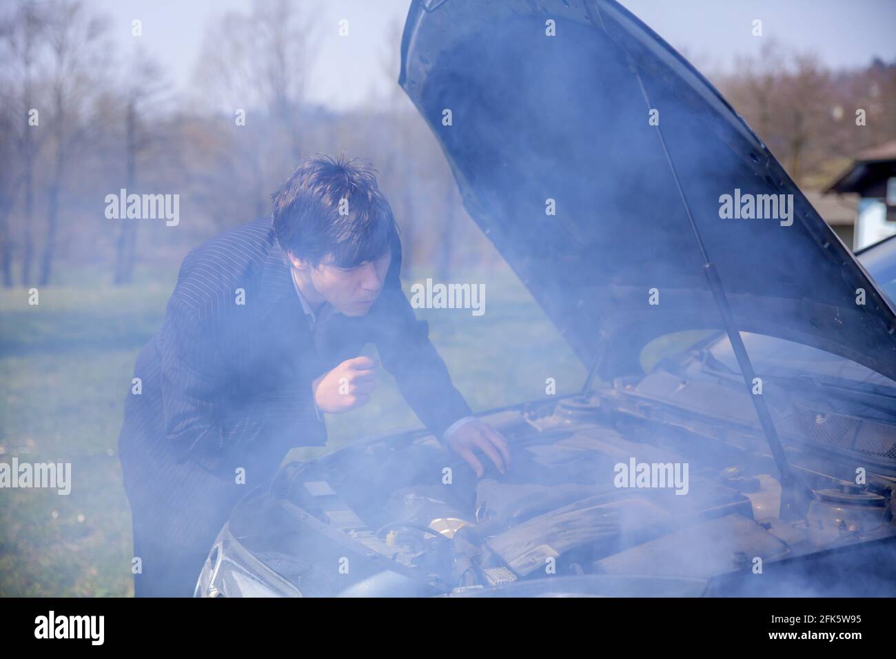 Worried driver attempting to repair the car coughing from the smoke ...