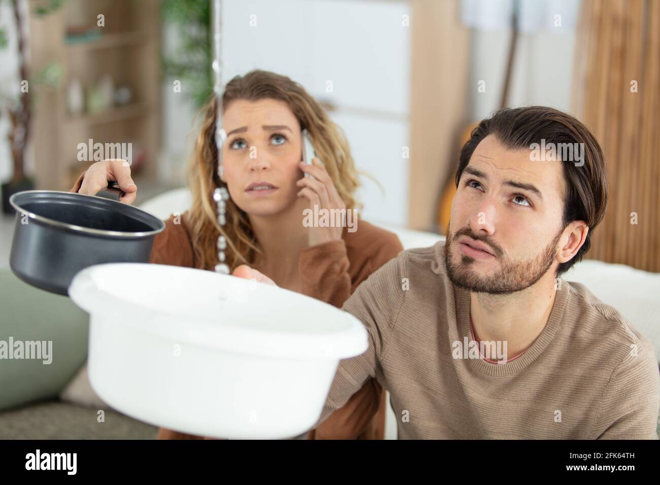 emotional couple collect water leaking from ceiling while phoning ...