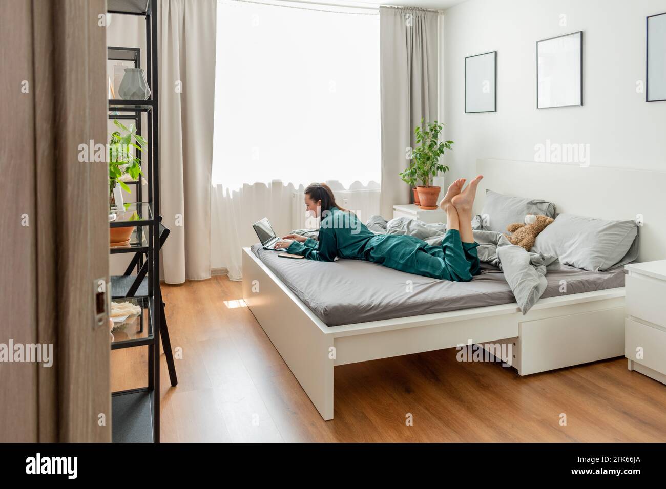 Young woman work at laptop while sitting on bed in bedroom. Concept of ...