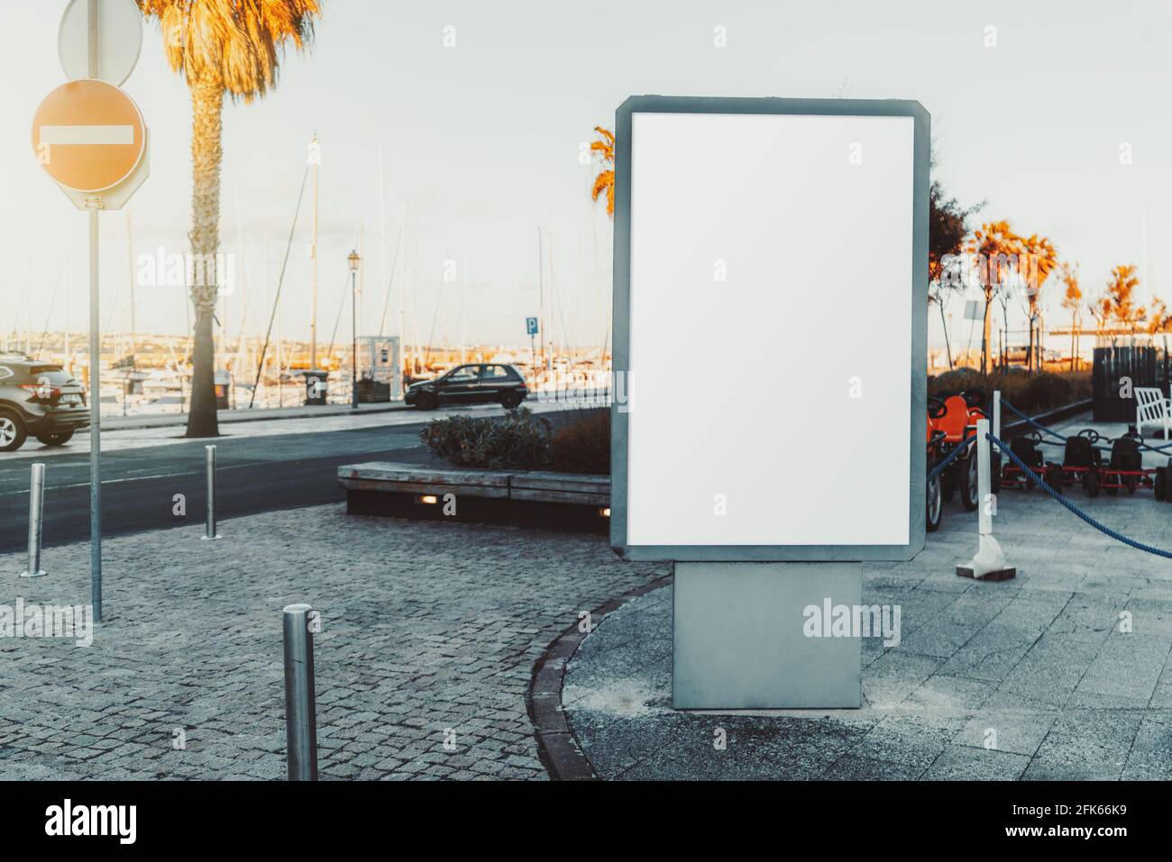 A vertical blank ad poster mockup on the sidewalk near the seaside; an ...