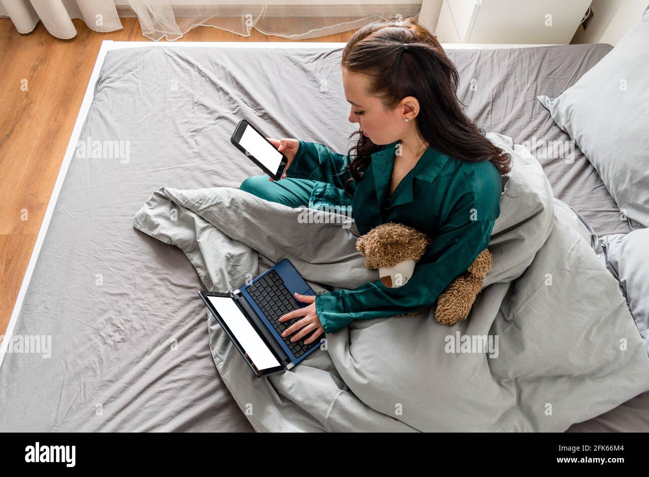Young woman work at laptop while sitting on bed in bedroom. Concept of ...