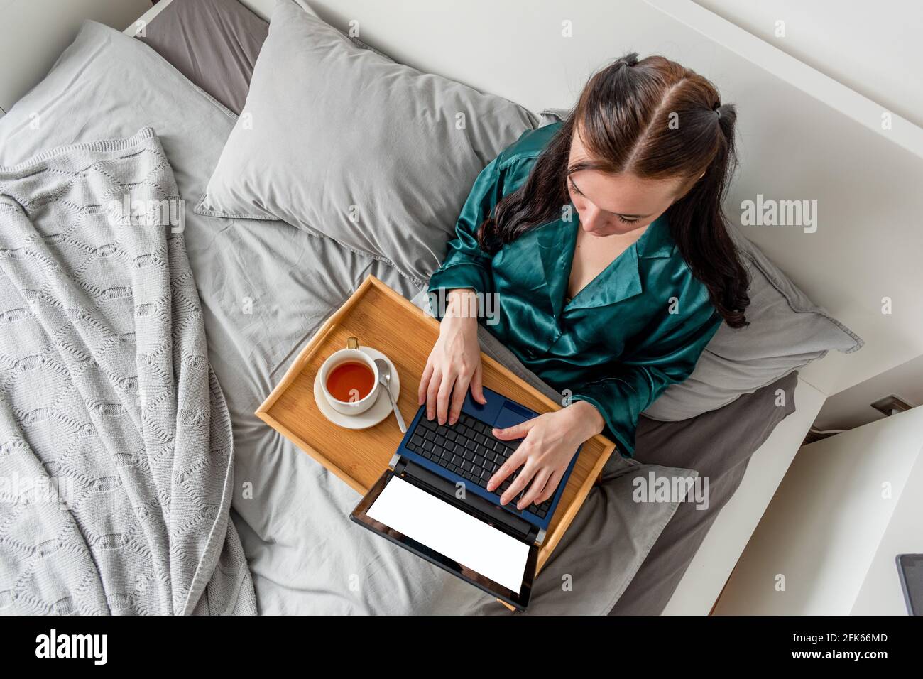 Young woman work at laptop while sitting on bed in bedroom. Concept of ...