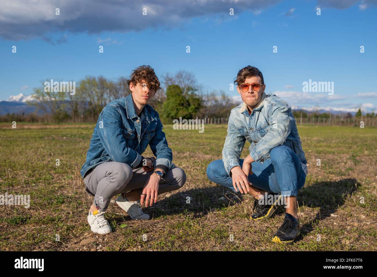 Two brothers dressed in denim jackets pose on a meadow squatting ...