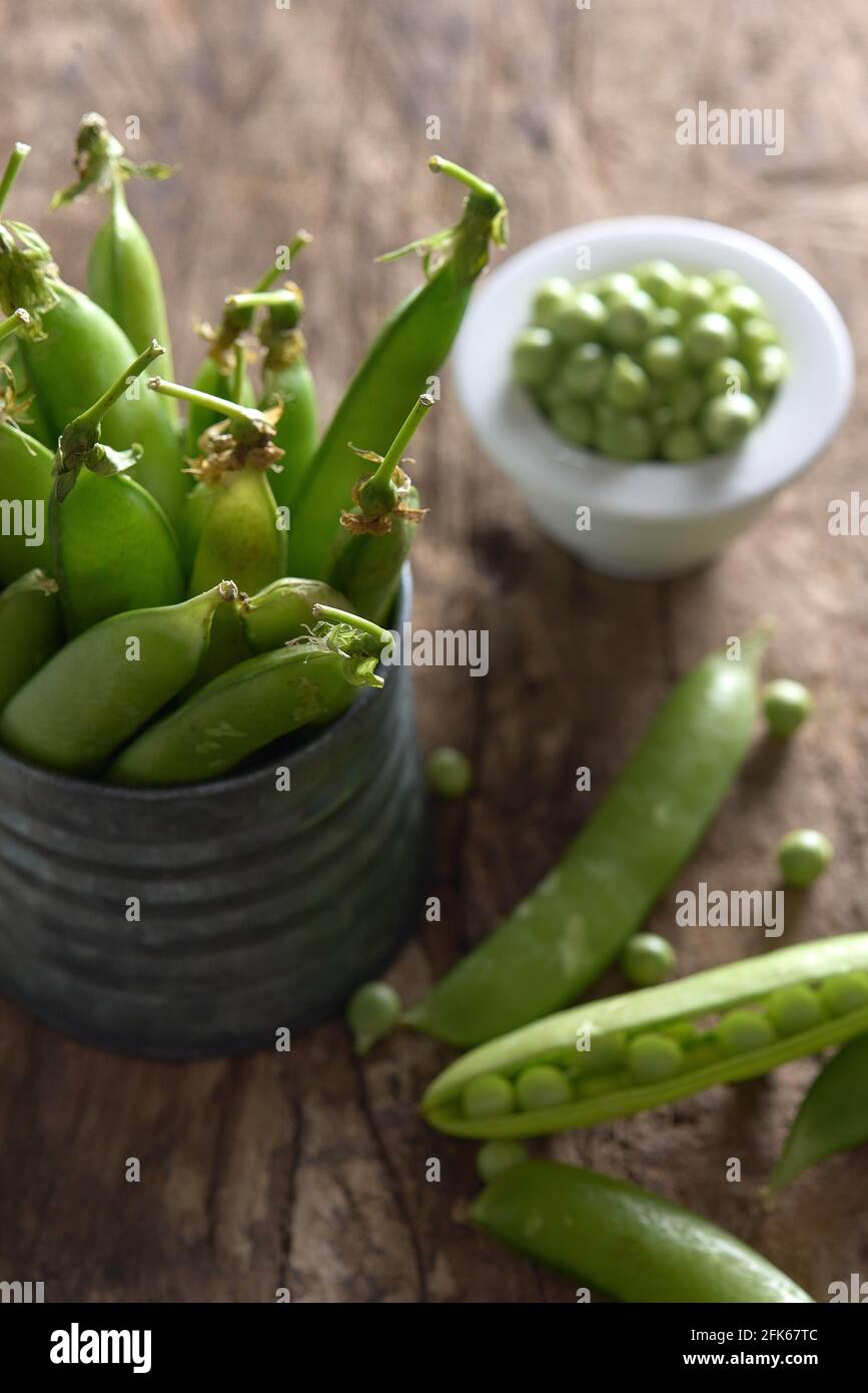 High angle shot of a ceramic bowl of peas next to pea pods in a metal ...